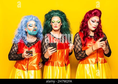 Surprised drag queens using mobile phone against yellow background ...