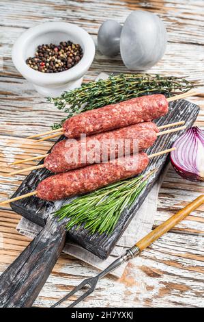 Raw kofta or lula kebabs skewers on a grill with herbs. Dark wooden ...