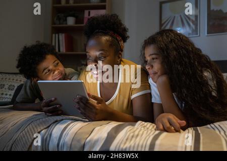 Careful middle-aged African American mother lying on bed and using ...