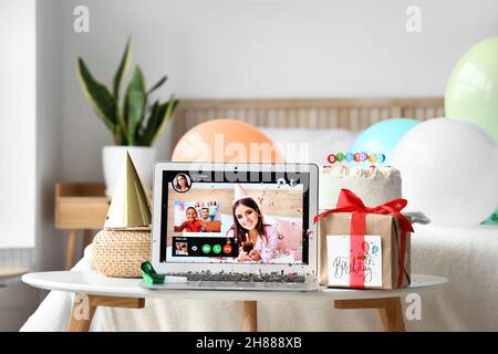 Laptop, gift and cake on table in room. Celebrating Birthday online due ...