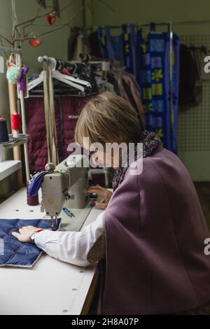 Person uses sewing machine to create clothing in a bright room at home ...