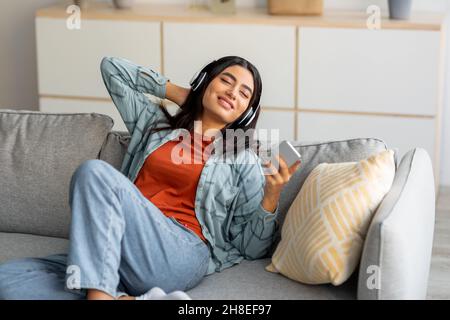 Young beautiful arab woman listening to music sitting on sofa at home ...
