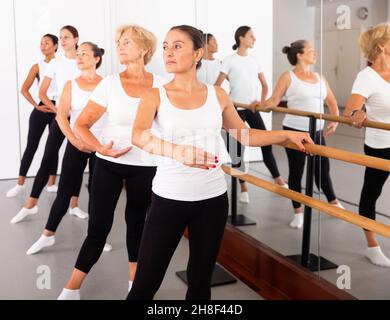 Female ballet trainer teaching group of dancers near ballet barre in ...