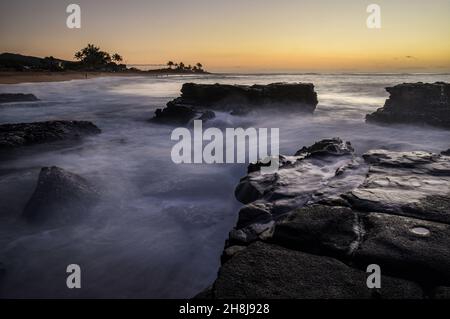 Sunrise as the surf crashes on and swirls around volcanic lava rocks ...