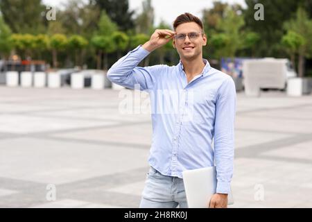 handsome young programmer in eyeglasses and headphones working with laptop and desktop computer ...