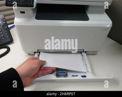 Woman loading paper into printer at white chest of drawers indoors ...