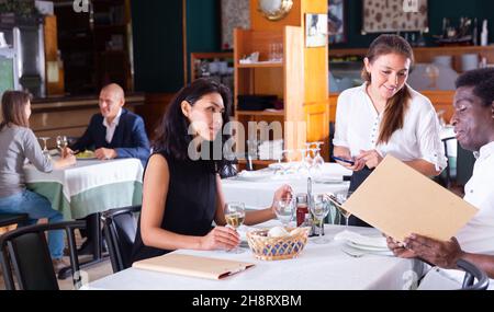 Polite young waitress helping with menu to African American Stock Photo ...