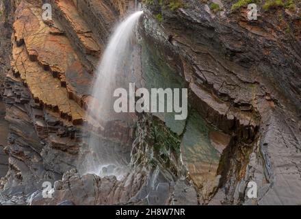 Waterfall against sandstone rock strata on beach at Sandymouth, near ...