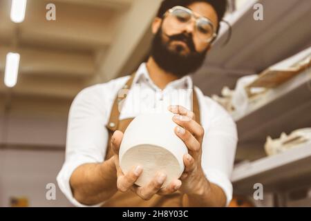 A young attractive male potter with a beard and mustache works in his ...