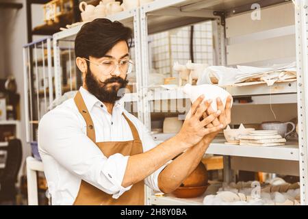 A young attractive male potter with a beard and mustache works in his ...