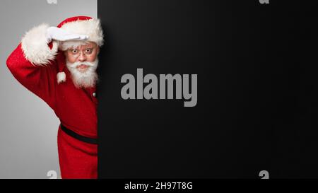 Santa Claus holding hand near ear standing with black billboard Stock ...