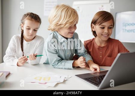 Schoolboy sitting at desk and typing on laptop, he learning to use ...