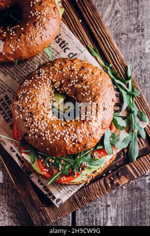 Bagels with cream, avocado, tomatos and arugula on wooden board ...