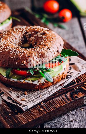 Bagels with cream, avocado, tomatos and arugula on wooden board ...