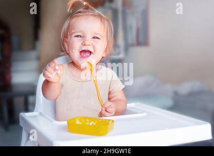 Baby's first meal. The child eats on his own with a spoon. Kitchen ...