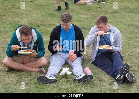 Three festival goers having lunch on the grass on the first day of ...