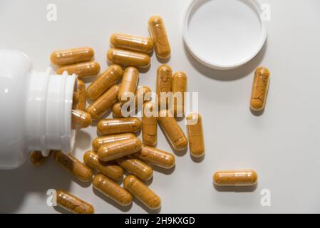 Transparent capsules with yellow powder in a white bottle on white ...