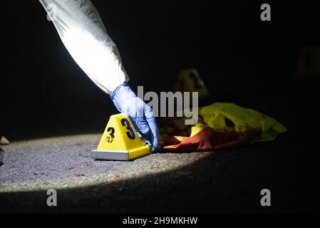 Forensics placing evidence marker number three by bloodied reflective ...