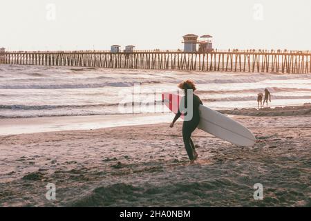 Woman carrying surfboard at sunset by pier Stock Photo - Alamy