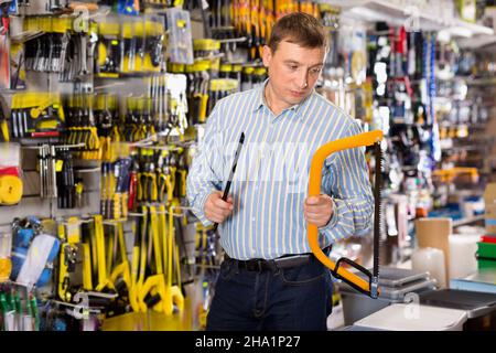 Confident man is choosing hacksaw in tools store Stock Photo - Alamy