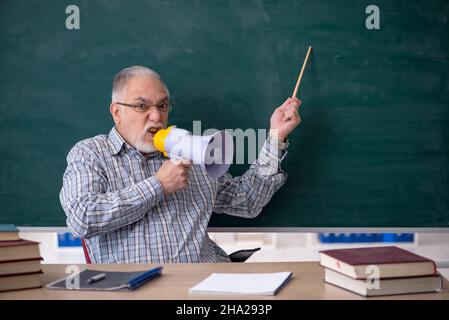 Aged male teacher holding megaphone in the classroom Stock Photo - Alamy