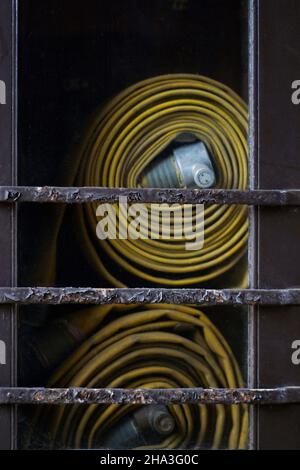 Rolled industrial fire hoses with metal couplings are laying on a rusty ...