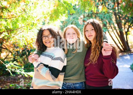 Three pretty tween girls laughing together outdoors in fall colors ...