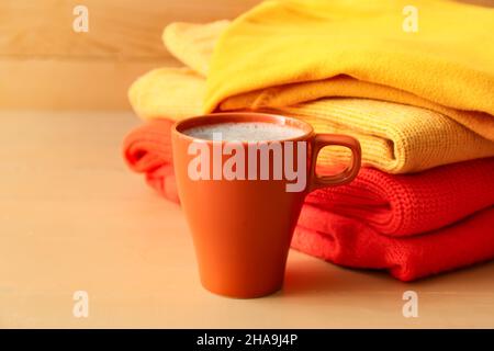 Stack of different cozy sweaters and cup of coffee on wooden background ...