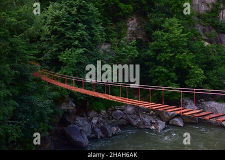 Suspended rope bridge without people with rocky banks over a mountain ...