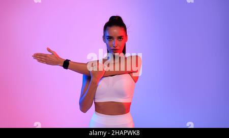 Fit lady stretching arms wearing fitness watch exercising, studio shot ...