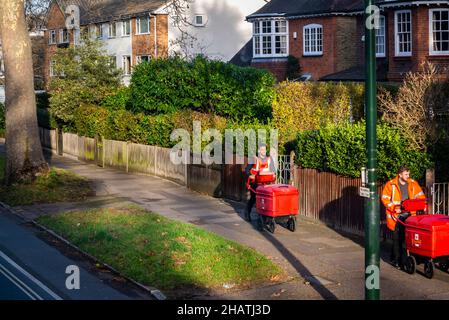 Two postmen pushing their trolleys in a suburban street, London ...