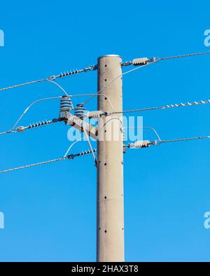 Photograph of a concrete telephone post and cables against a blue sky ...
