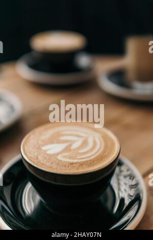 Cups of aromatic foamy cappuccino with latte art served on wooden table ...