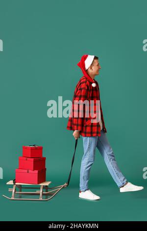 Young man with gifts on sledges against green background. Christmas ...