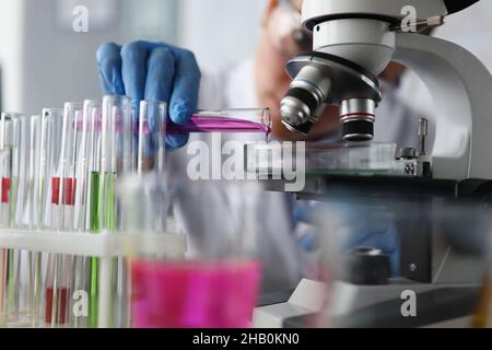 Female scientist pouring pink sample liquid on glass container under ...