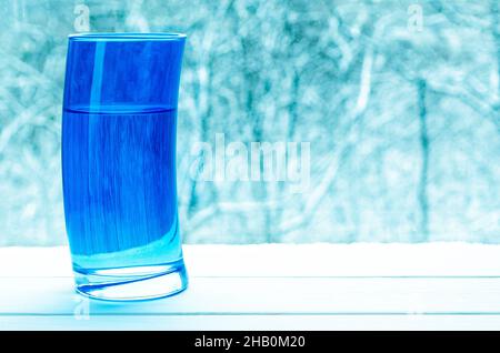 Deformed blue glass with clear spring water on the background of a ...