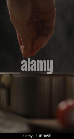 man adding salt to boiling water in saucepan with strong backlight ...