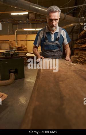 Serious woodworker processing wooden plank in workshop Stock Photo - Alamy