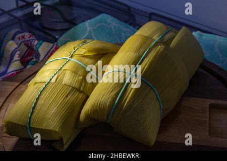 Two pamonhas wrapped in corn husks and tied with pink string on glass ...