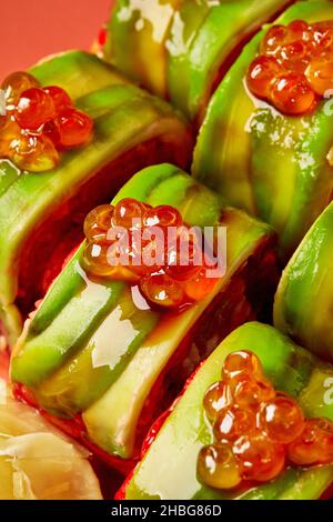 A closeup of a sushi roll topped with red caviar and garnish on a plate ...