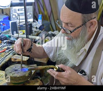 A Jewish silversmith and master craftsman works polishing the base of a ...
