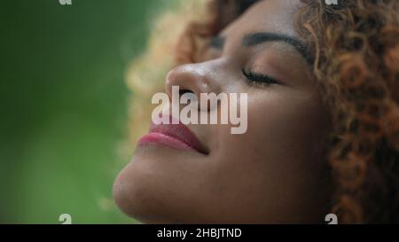 African woman taking a deep breath outside in nature looking up at sky ...