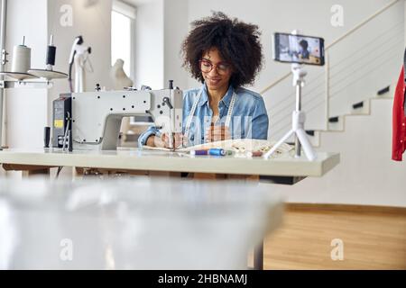 Positive African-American dressmaker shoots tutorial at workplac Stock ...