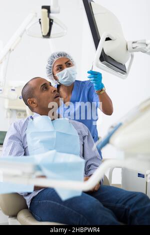 Orthodontist pointing at teeth radiography on monitor to show caries ...