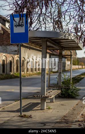 An empty public bus station with a rusty sign indicating the bus stop ...