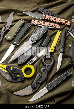A variety of folding and pocket knives lie on khaki fabric. A versatile ...