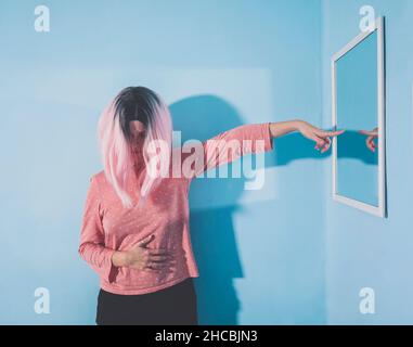 Woman with pink hair pointing at mirror on blue wall Stock Photo - Alamy