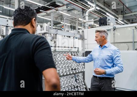 Businessman sharing expertise with coworker over equipment in industry ...