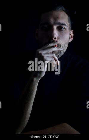 portrait of a young man who is inhaling the smoke of a cigarette while ...