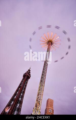 Blackpool Tower with a spinning funfair ride lit up with the ...